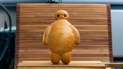 Bread in the shape of Baymax, standing on a wooden baker's paddle