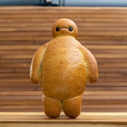 Bread in the shape of Baymax, standing on a wooden baker's paddle
